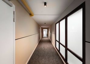 Corredor com piso coberto por carpete, paredes brancas e grandes janelas com painéis de vidro fosco.