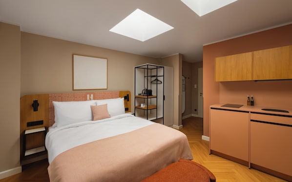 Quarto com cama, mesa de cabeceira, guarda-roupa, armário suspenso, cozinha compacta e claraboia.