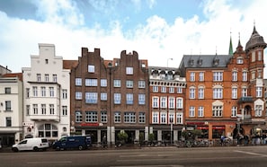 Rua com edifícios históricos, incluindo um prédio branco com a placa 'YUME' e um prédio marrom com a placa 'BLOCK HOUSE'.