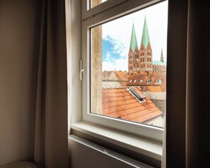 Janela com vista para um edifício com duas torres pontiagudas e telhado de telhas vermelhas.