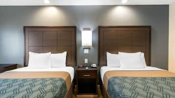 Quarto de hotel com duas camas, mesa de cabeceira e luminária fixa na parede.