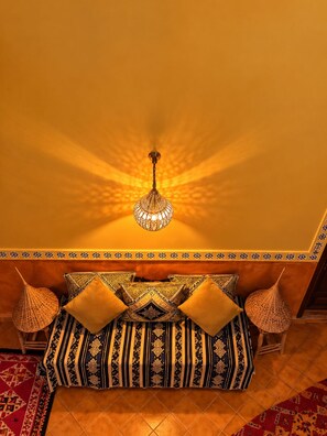 Quarto com sofá estampado, almofadas decorativas, luminária pendente e detalhe estampado na parede.