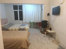 Quarto de hotel com duas camas, televisão, escrivaninha e janela com cortinas.