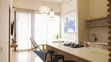 Uma cozinha moderna com uma ilha central, banquetas, um espaço de refeições com uma cadeira e uma grande janela com cortinas.