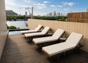Uma área de lounge no terraço, com piso de madeira e poltronas confortáveis com almofadas brancas.