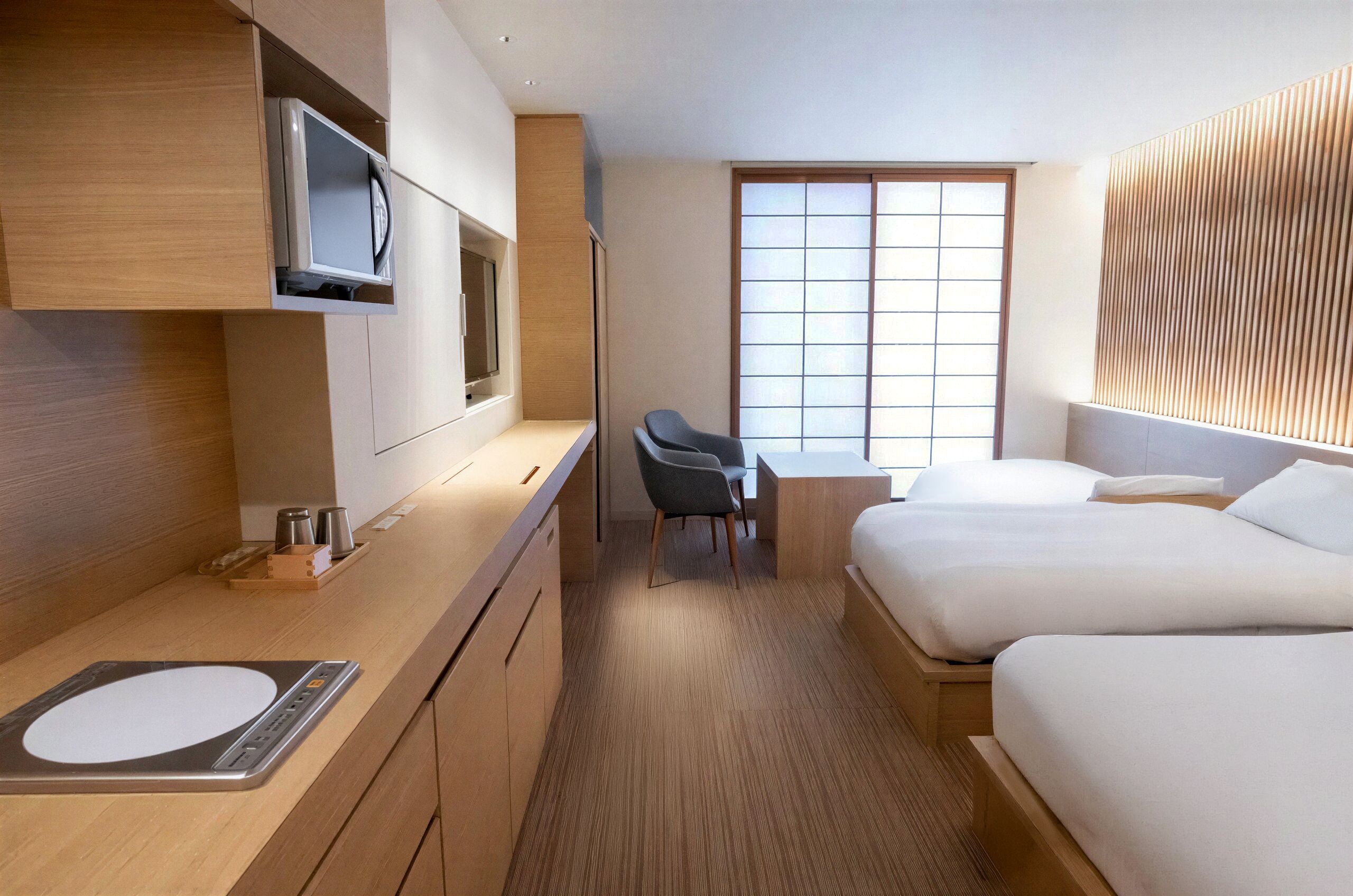 Quarto de hotel com cama, escrivaninha, cadeira, micro-ondas e janela com persianas.