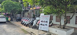 Fileira de scooters estacionadas em frente a um edifício com uma placa anunciando aluguel de scooters.