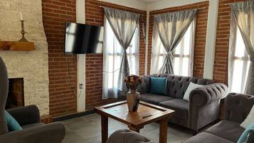 Uma sala de estar com parede de tijolos, TV de tela plana, conjunto de sofá, mesa de centro e lareira.