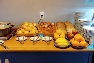 Buffet com diversos alimentos, incluindo pães, doces, frutas e uma panela de comida no fogão.