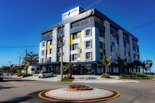 Um hotel moderno com um letreiro 'Candeias' em destaque, vários andares e uma área de entrada com paisagismo.