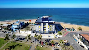 Hotel com vista para a praia, área de estacionamento e estrada com palmeiras.
