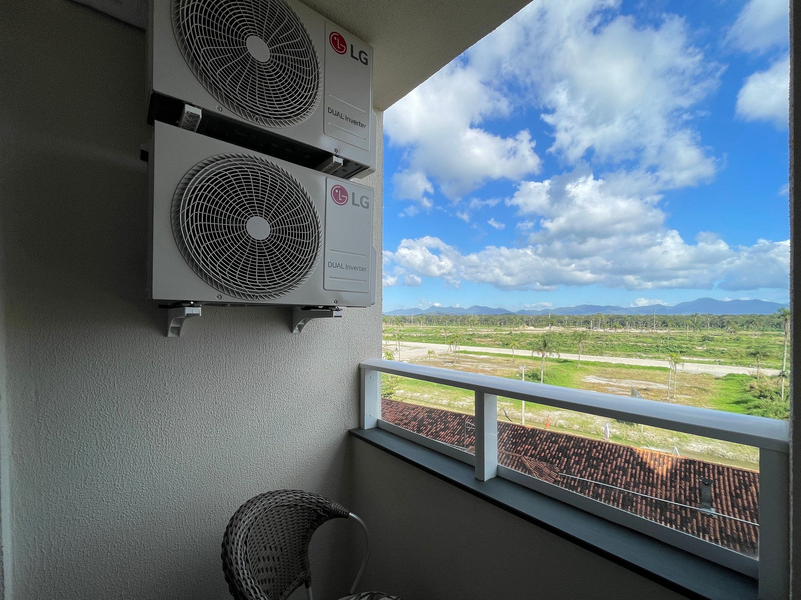 Varanda com duas unidades de ar condicionado LG Dual Inverter, uma cadeira de vime e vista para uma paisagem com montanhas e céu claro.