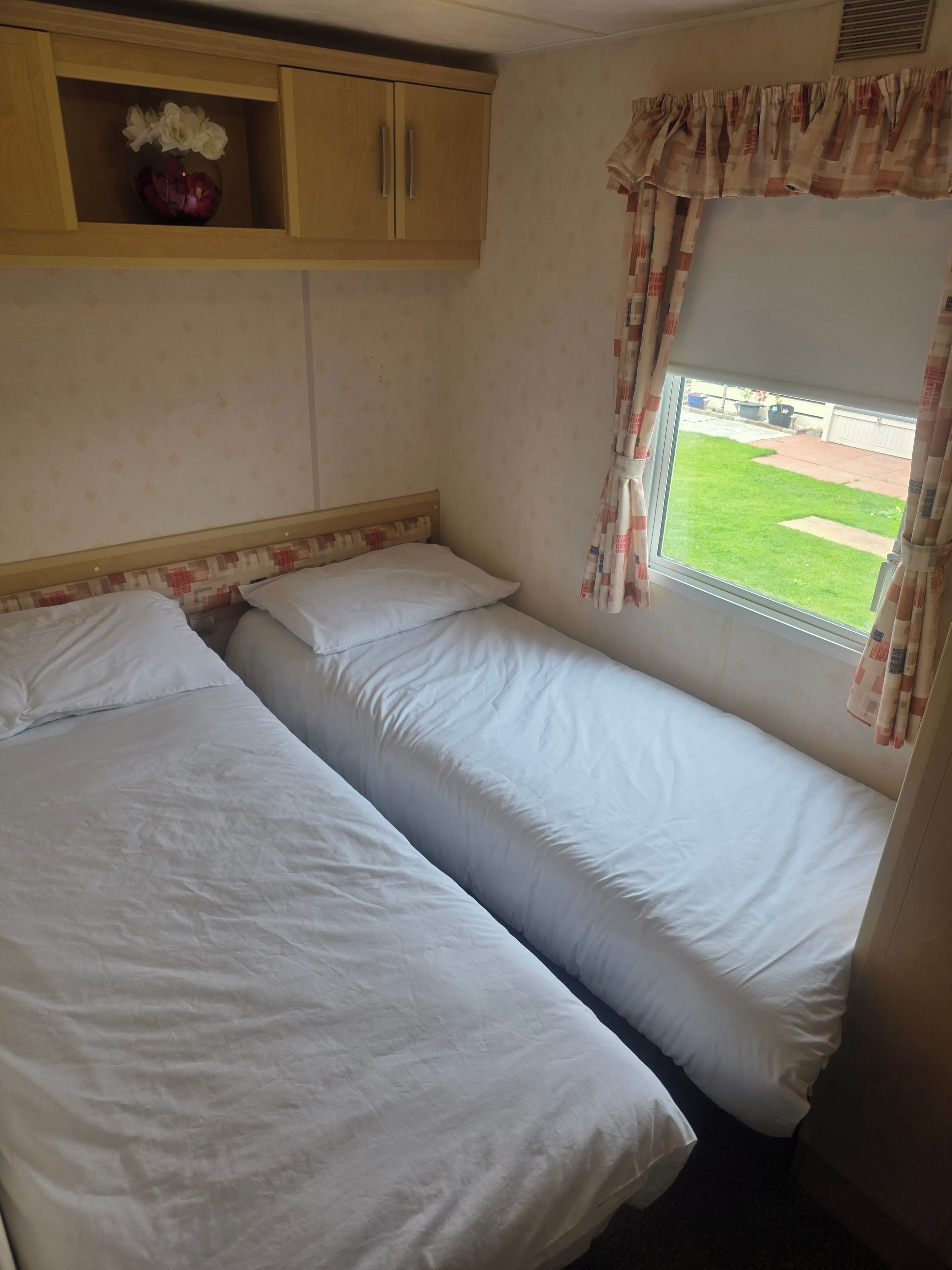 Quarto com duas camas, um armário de madeira e uma janela com cortinas.