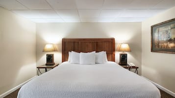 Quarto de hotel com uma cama grande, duas mesas de cabeceira com luminárias, uma cabeceira de madeira e um quadro na parede.