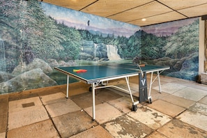 Uma mesa de pingue-pongue em um quarto com um mural de uma floresta e cachoeira.