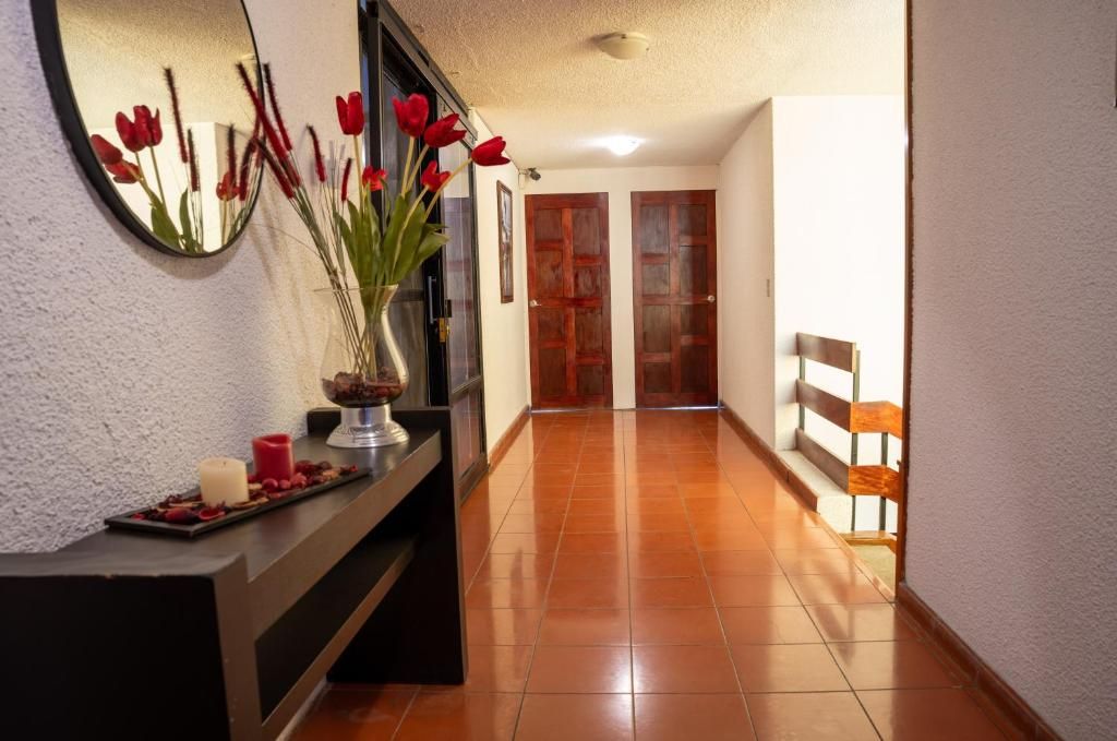 Um corredor com um espelho, um vaso de flores vermelhas e uma pequena mesa com velas.