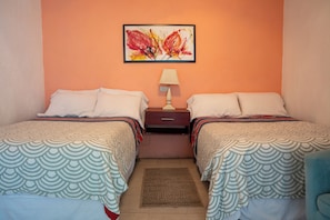 Quarto de hotel com duas camas, uma mesa de cabeceira, uma luminária e um quadro na parede.