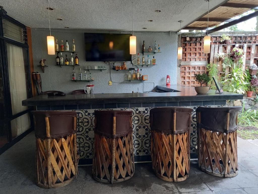 Uma área de bar com balcão extenso, banquetas e uma TV fixada na parede.