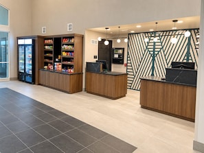 Uma área de recepção com balcão, geladeira abastecida com bebidas e parede estampada.