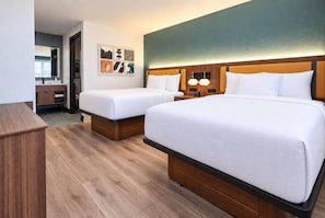 Quarto de hotel com duas camas, cabeceira de madeira, mesa de cabeceira, espelho e luminária fixada na parede.