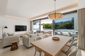 Sala de estar moderna com televisão de tela plana, área de jantar com mesa de madeira e varanda com mobiliário externo.