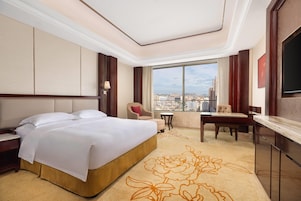 Quarto de hotel com uma cama grande, uma escrivaninha, uma cadeira e vista para a cidade.