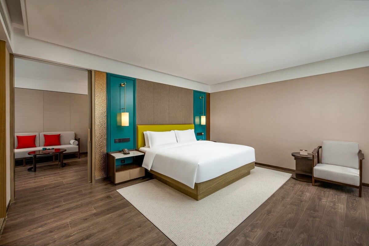 Quarto de hotel com uma cama grande, um sofá, uma cadeira, uma mesa de cabeceira e um abajur.