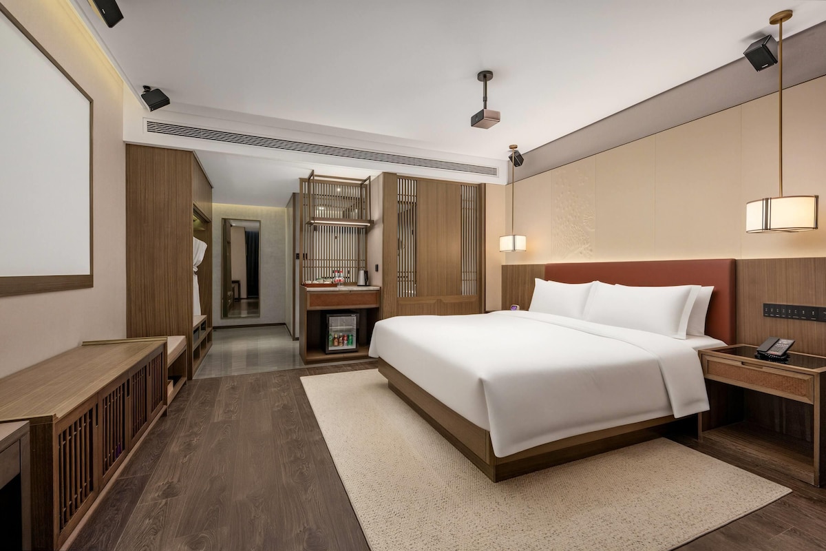 Quarto de hotel com cama grande, escrivaninha, guarda-roupa e minibar.