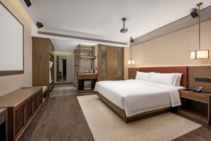Quarto de hotel com cama grande, escrivaninha, guarda-roupa e minibar.