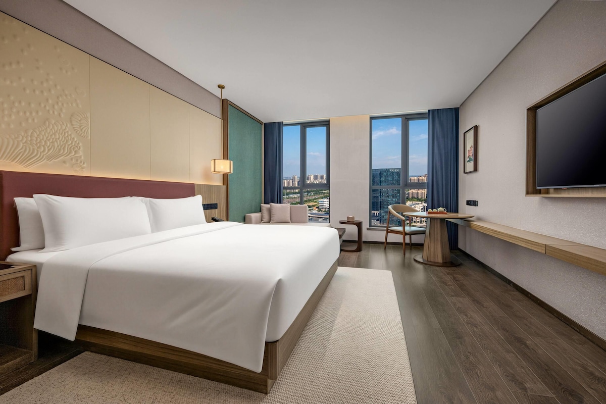 Quarto de hotel com uma cama grande, uma escrivaninha, uma cadeira e uma televisão.