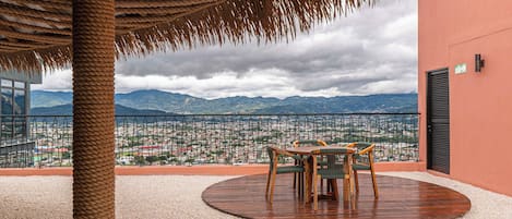 Terraço com vista para um horizonte urbano e montanhas, com uma mesa e cadeiras de madeira redondas.