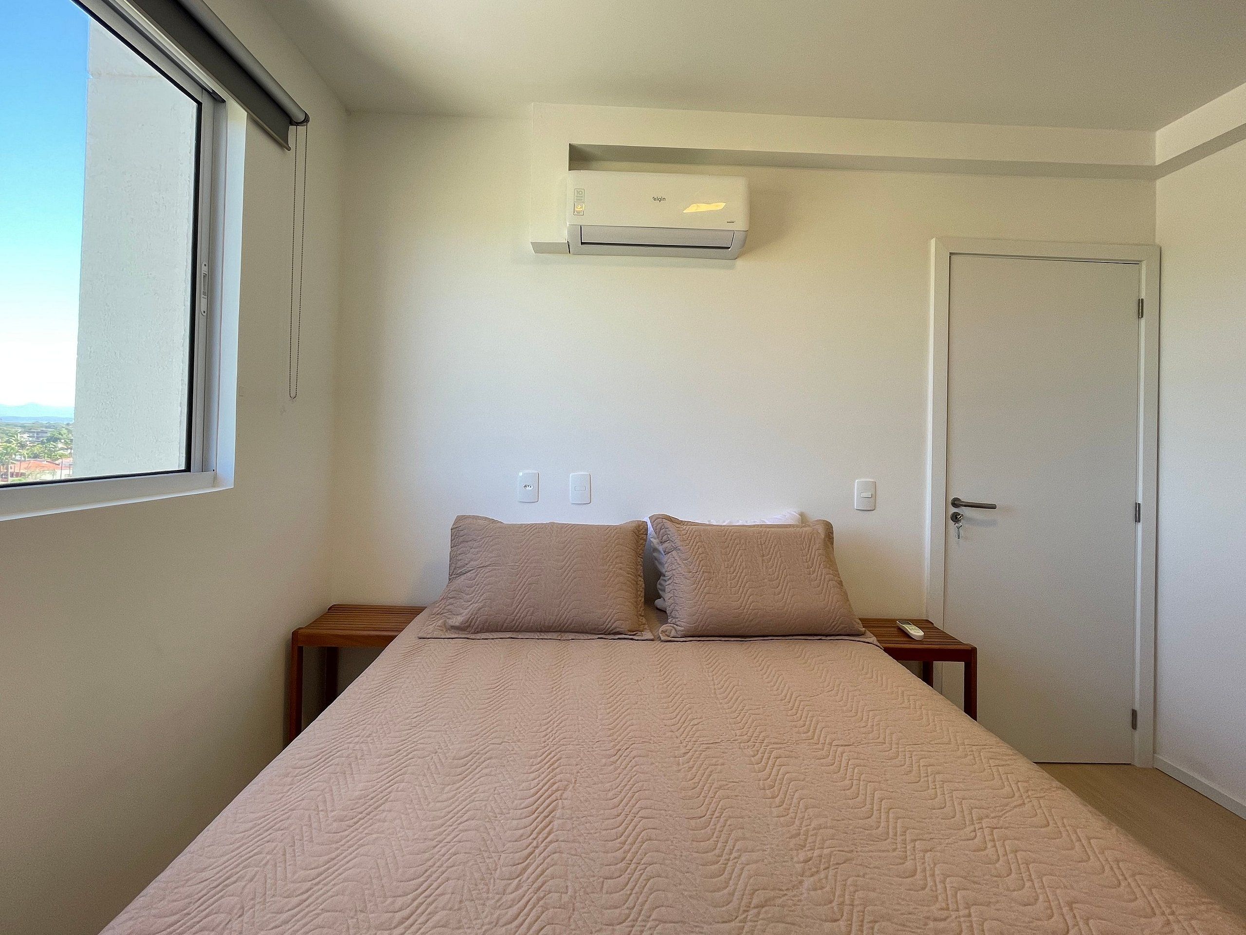 Quarto com cama, janela, ar-condicionado e porta.