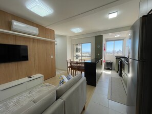 Uma sala de estar moderna com televisão de tela plana, um sofá, área de jantar com cadeiras e cozinha equipada com geladeira e fogão.