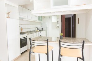 Cozinha com armários brancos, fogão, micro-ondas e dois banquetas altas.