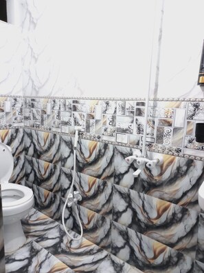 Uma casa de banho com design de azulejos marmorizados nas paredes e no chão, uma sanita branca e uma área de duche.