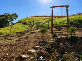 Paisagem rural com uma construção de madeira, degraus subindo uma colina e céu claro.