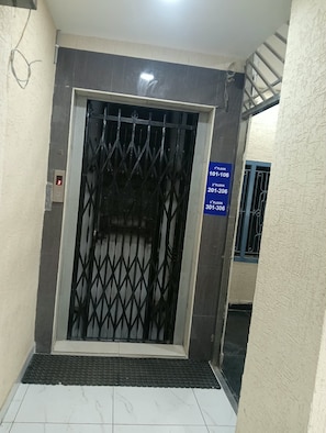Um elevador com portão de metal, indicador digital de andares e placa indicando os números dos pisos.