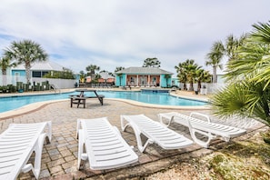 Piscina com espreguiçadeiras e mesa de piquenique, cercada por palmeiras e edifícios.
