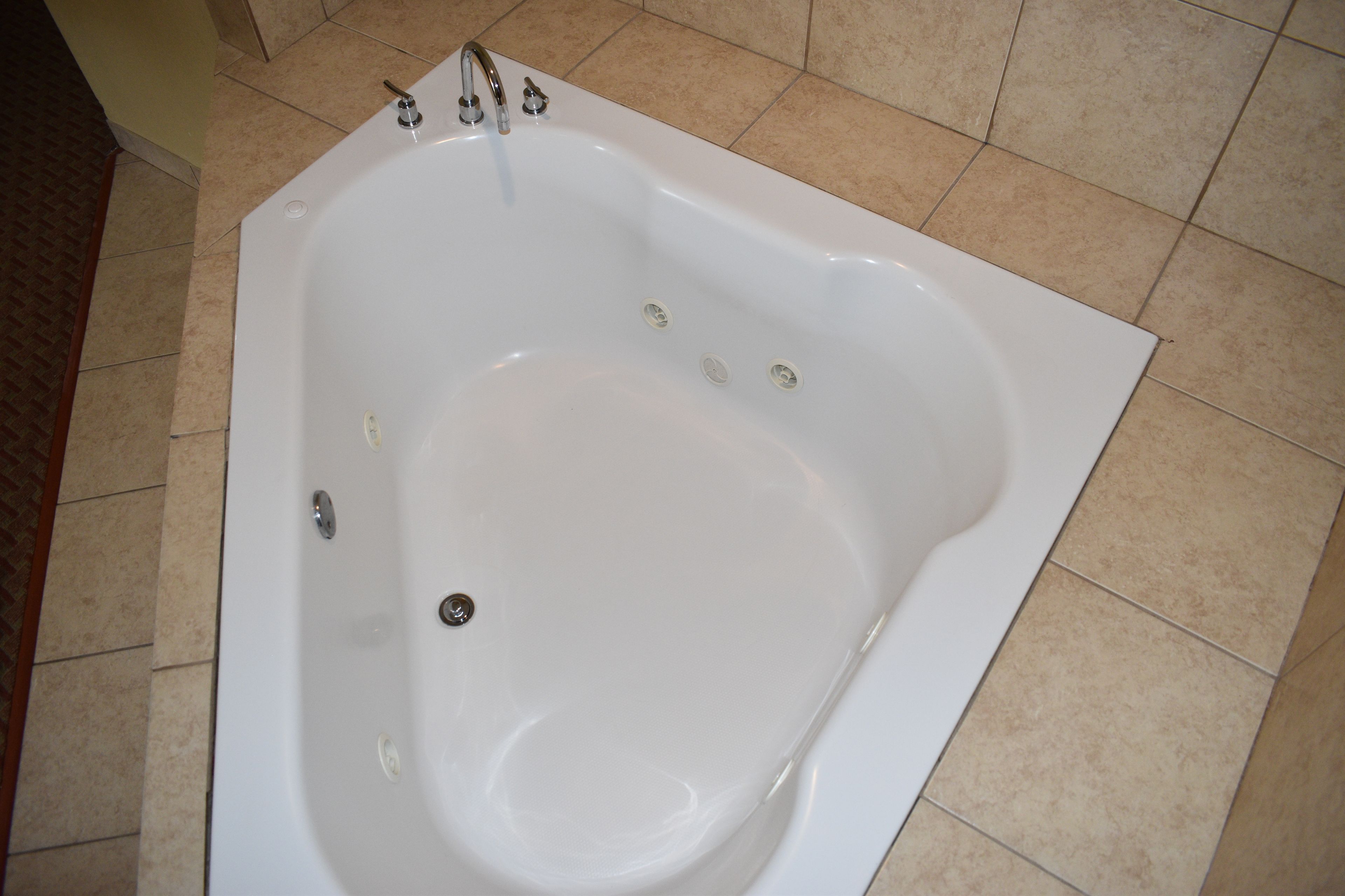 Uma banheira branca com uma torneira e um ralo, diante de um chão revestido de azulejos.