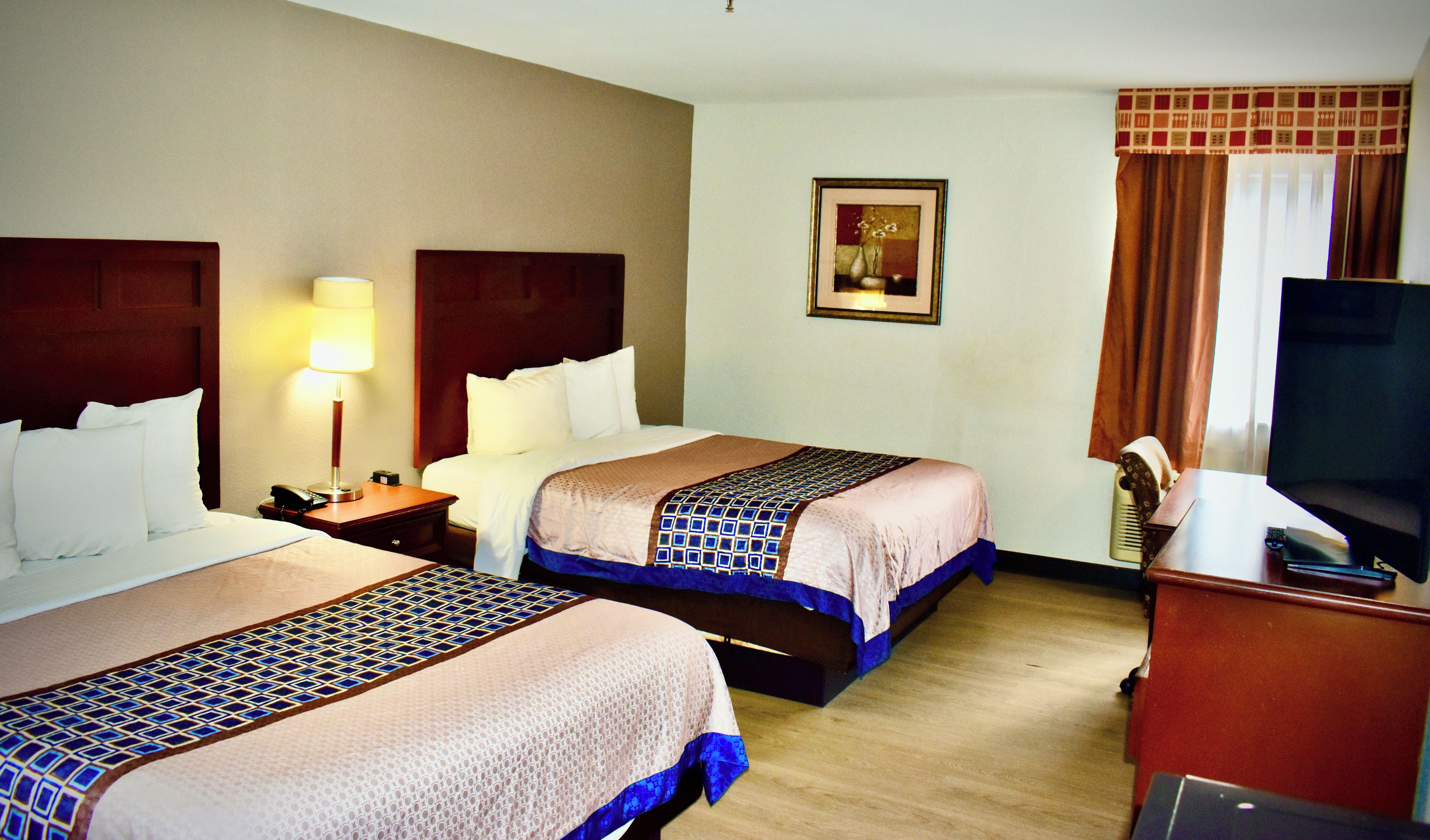 Quarto de hotel com duas camas, televisão, escrivaninha e um quadro na parede.
