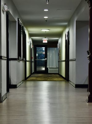Um corredor com piso coberto de carpete, portas em ambos os lados e uma placa de saída na parede.