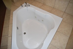 Uma banheira branca com uma torneira e um ralo, diante de um chão revestido de azulejos.
