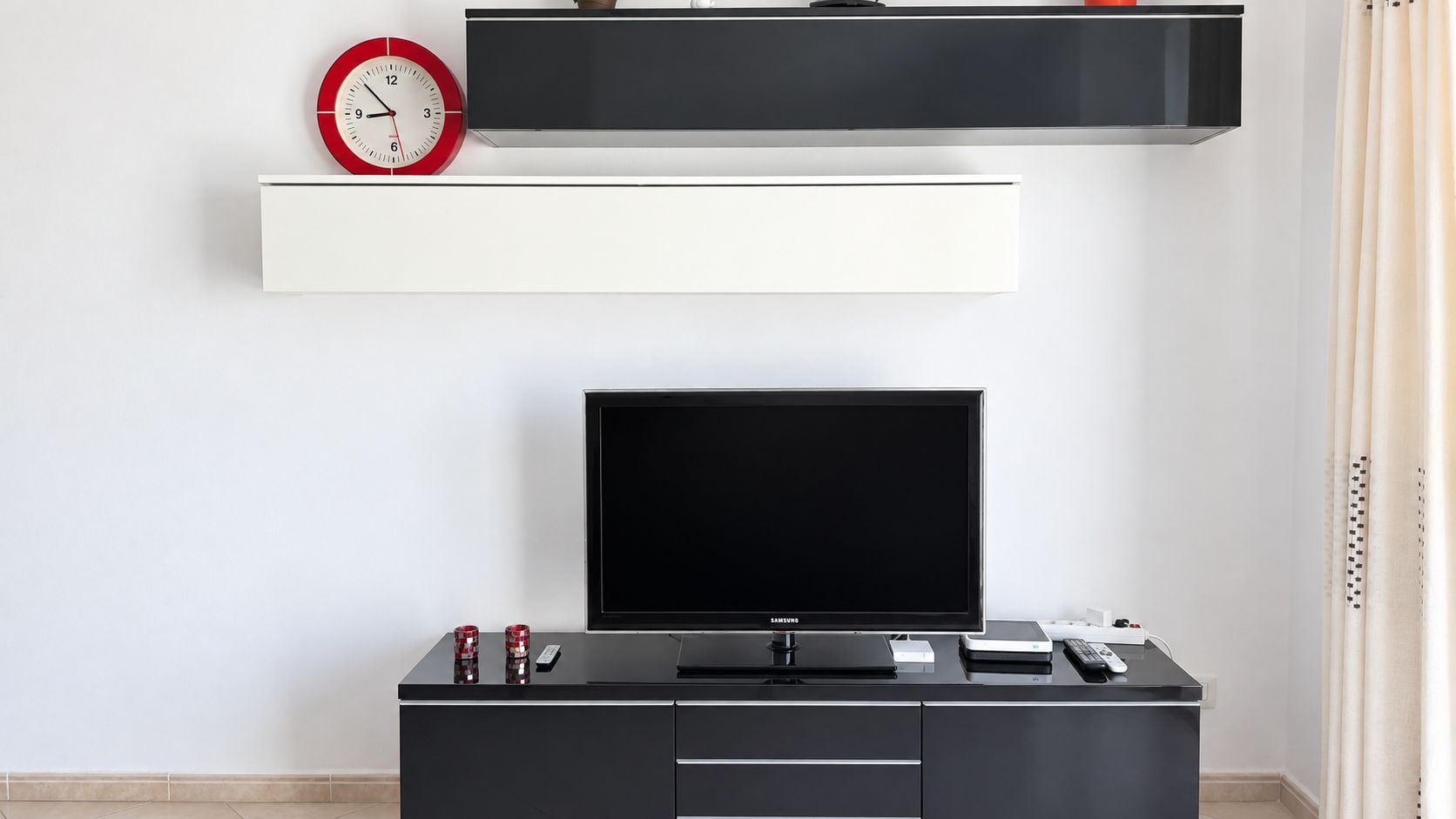 Uma sala de estar moderna com televisão de tela plana, um relógio e uma mesa de centro com dispositivos eletrônicos.