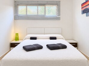 Quarto de hotel com cama, duas mesas de cabeceira, janela com persianas e um quadro na parede.