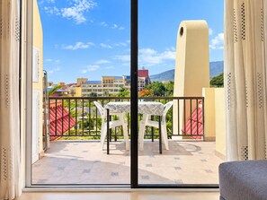 Uma varanda com mesa e cadeiras, vista de edifícios e vegetação, e uma montanha ao longe.