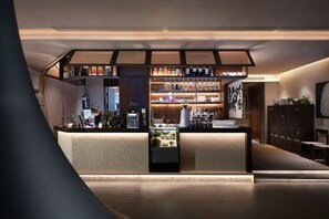 Uma área de bar com balcão, prateleiras com garrafas e uma vitrine com comida.