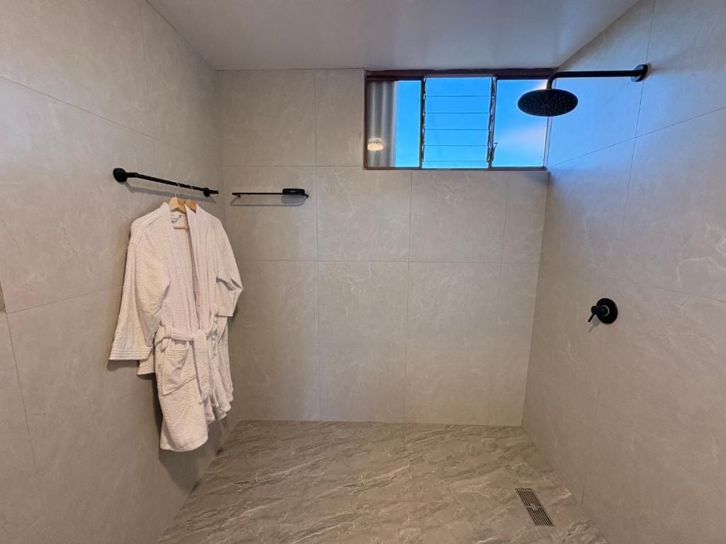 Chuveiro com porta de vidro, porta-toalhas com toalha branca e uma pequena janela acima do chuveiro.