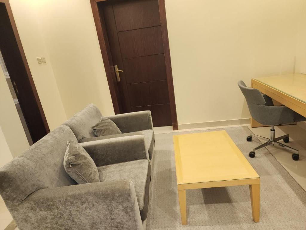 Um quarto com sofá cinzento, mesa de centro de madeira e escrivaninha com cadeira.