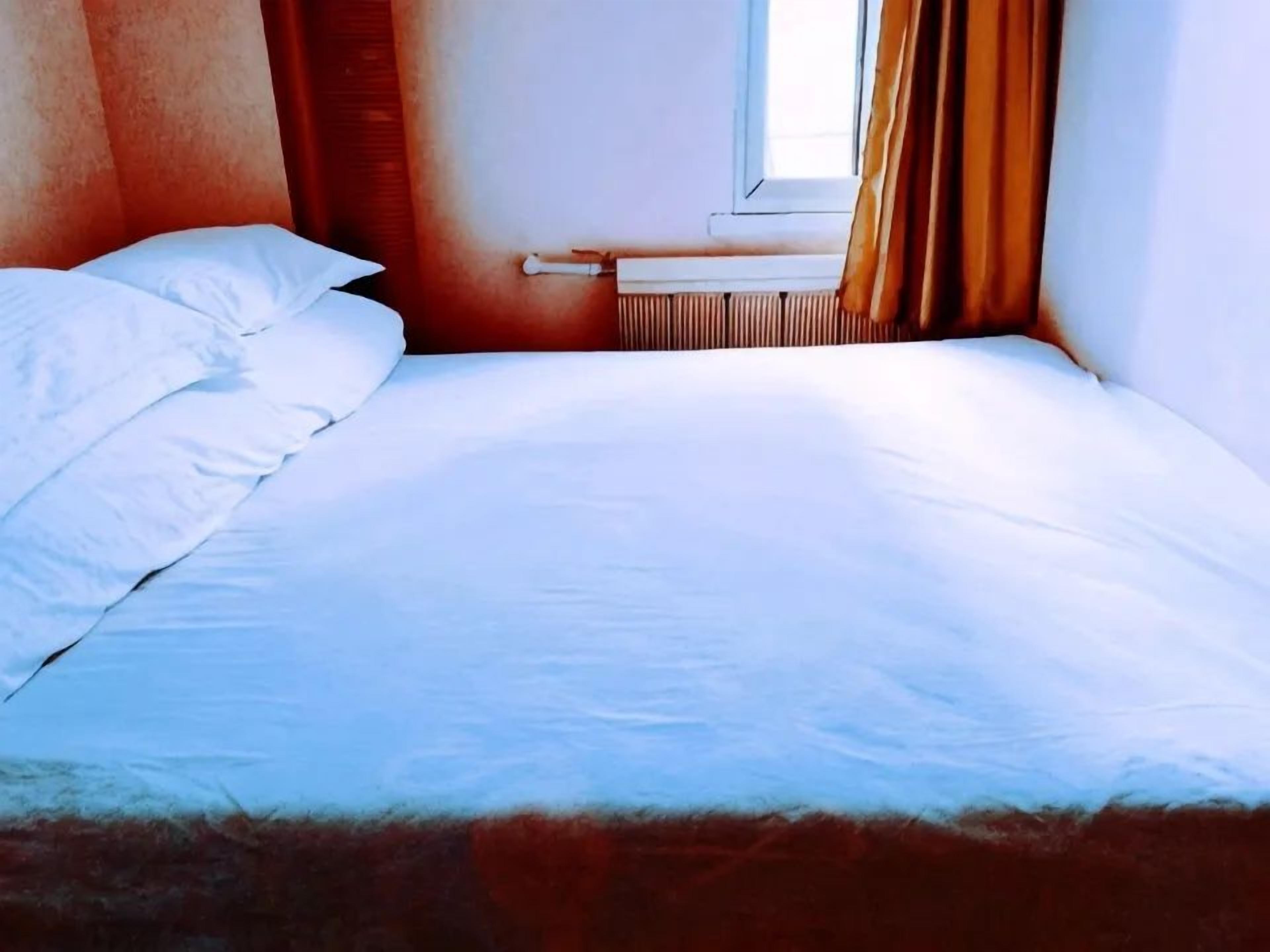 Cama com lençóis brancos em quarto com janela e cortinas.