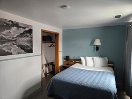 Quarto de hotel com cama, mesa de cabeceira, luminária, guarda-roupa e um quadro na parede.